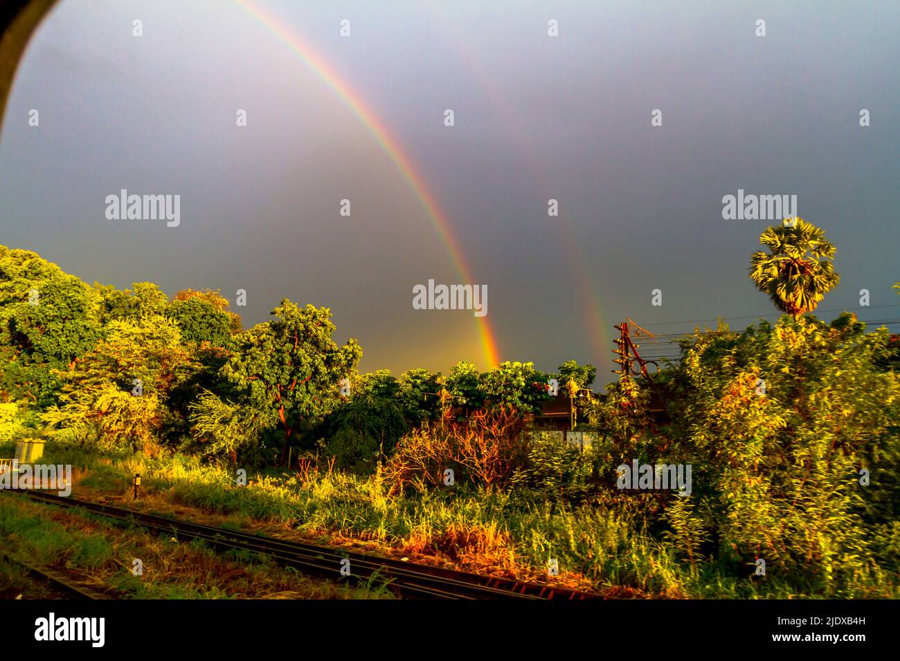 Rainbow outside of train window in Thailand. Storm clouds are dark ...