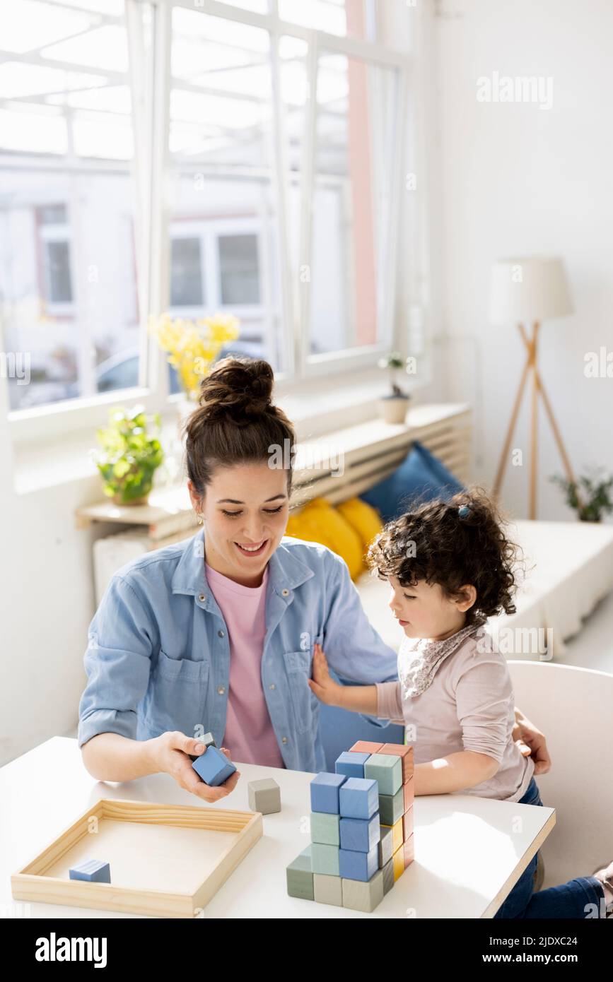 Mother sitting at table playing with daughter with building bricks ...