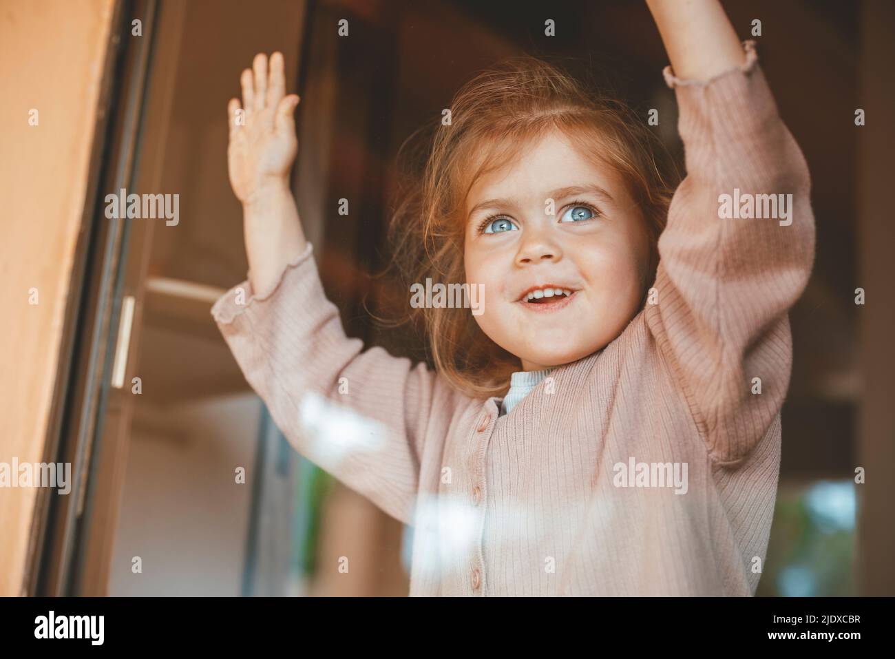 Happy cute girl at home looking out through glass window Stock Photo ...
