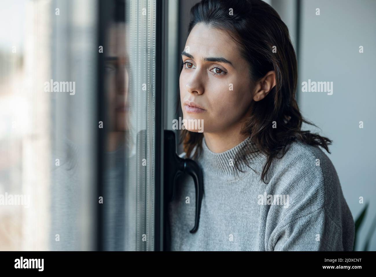 Sad woman looking out through window at home Stock Photo - Alamy