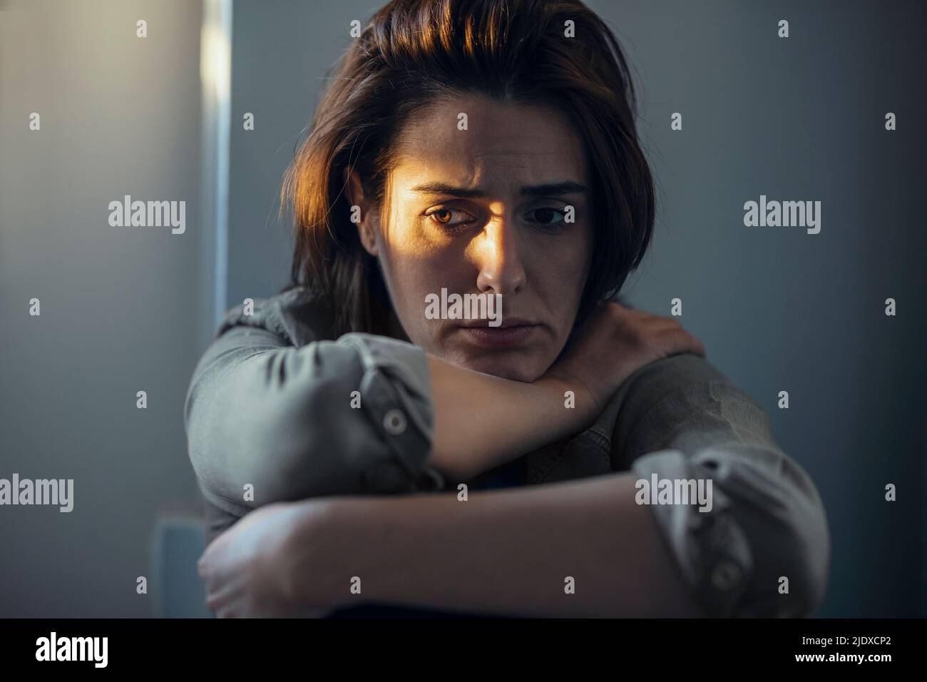 Worried woman sitting with sunlight on face at home Stock Photo - Alamy