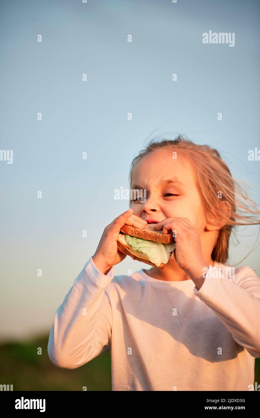 Girl eating sandwich in front of sunset sky Stock Photo - Alamy