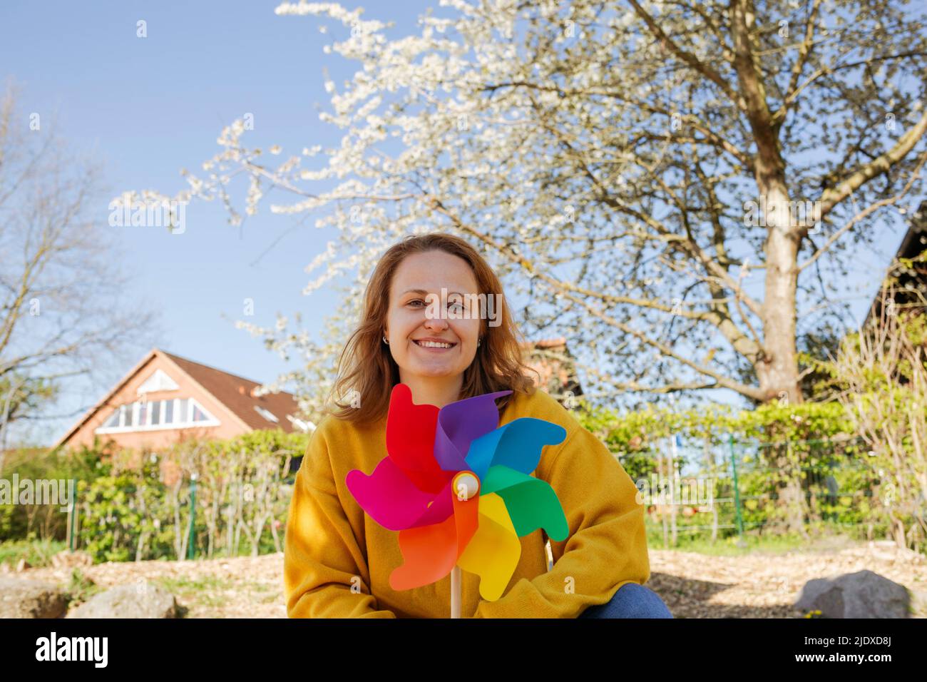 Happy woman with pinwheel toy sitting in front of tree at playground ...