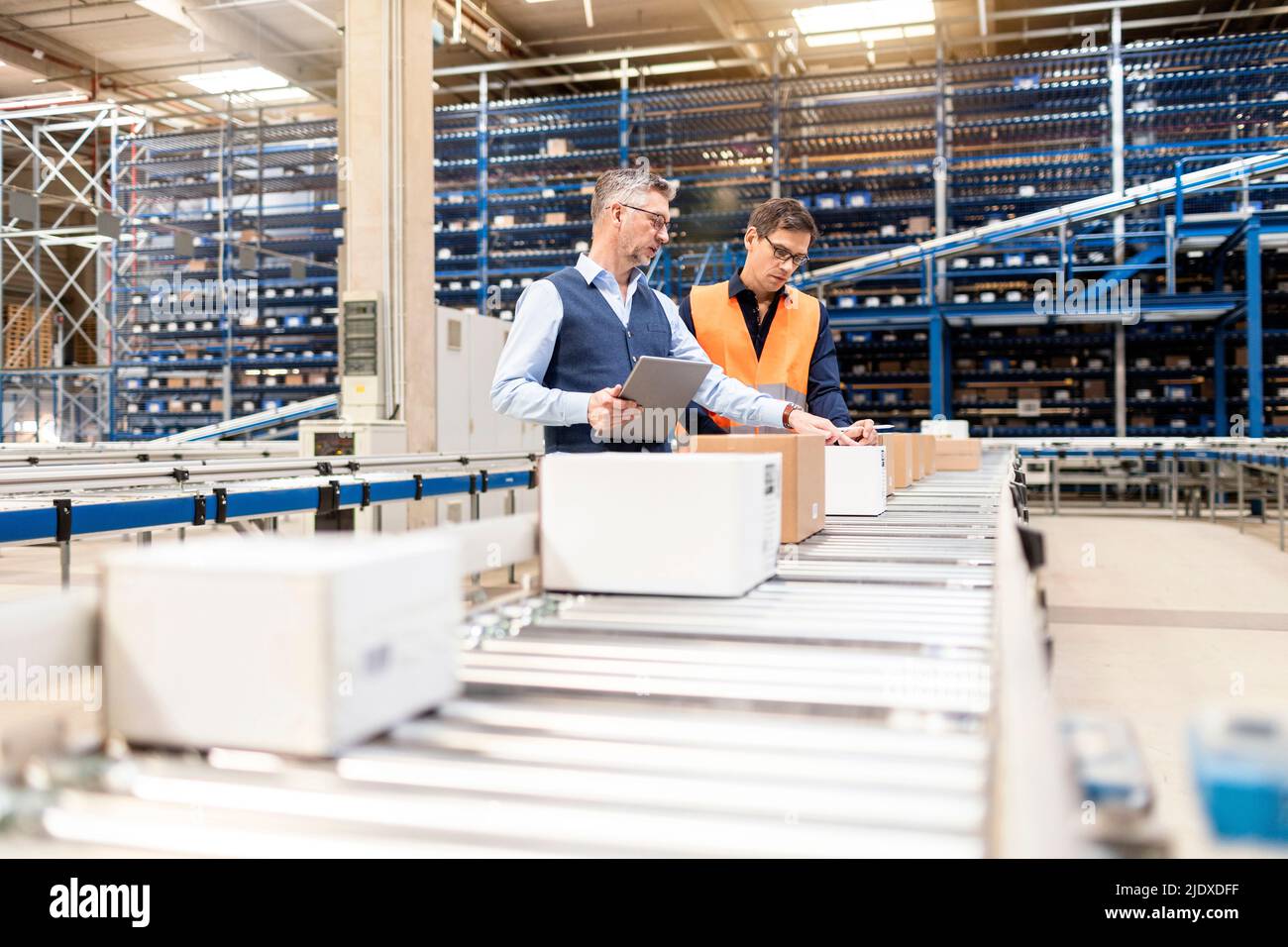 Manager discussing over cardboard boxes with colleague by conveyor belt ...