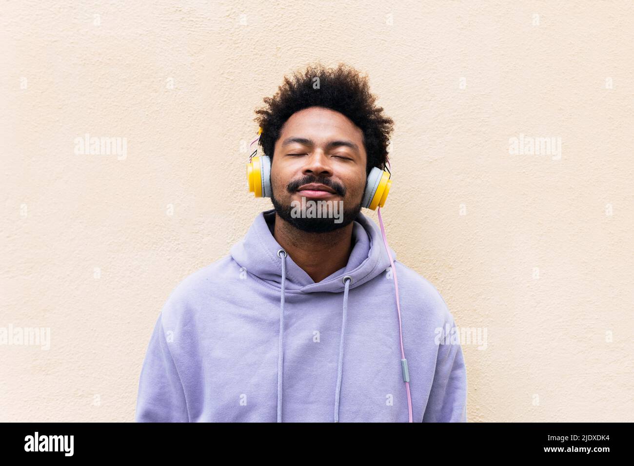 Man enjoying music listening through headphones in front of cream ...