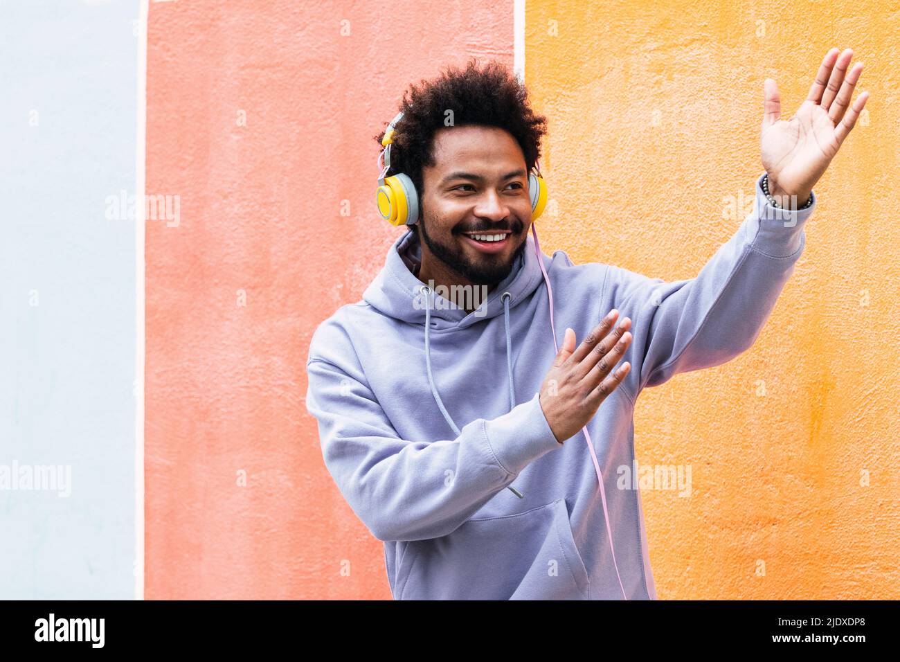 Smiling man enjoying music listening through headphones in front of ...