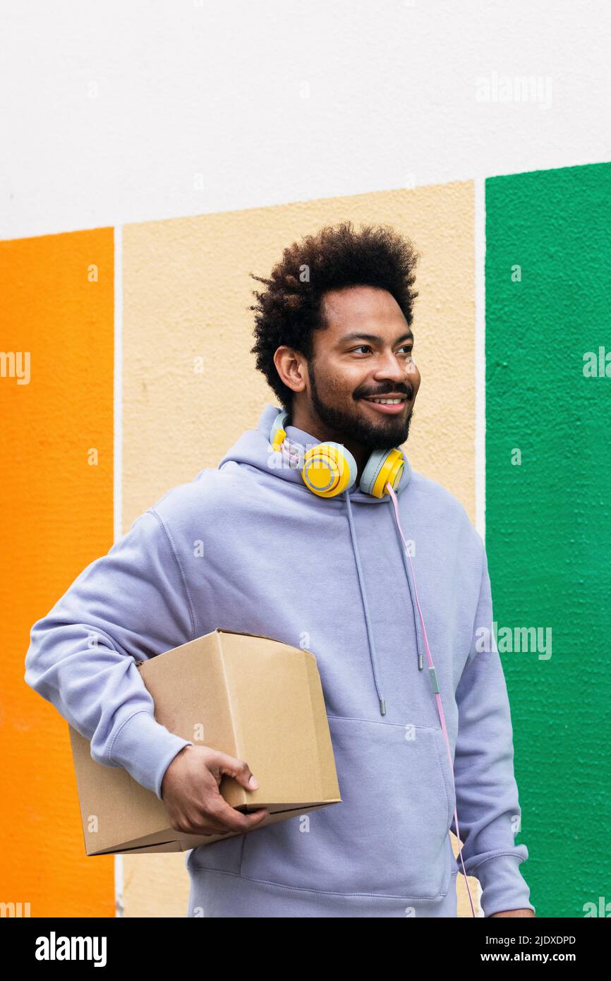 Smiling delivery man holding box in front of colorful wall Stock Photo ...