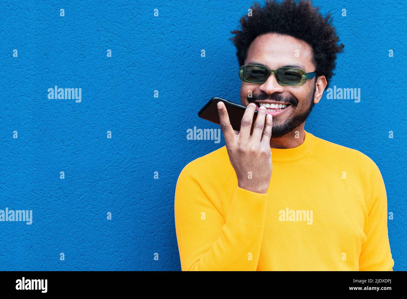 Smiling man talking on mobile phone through speaker in front of blue ...