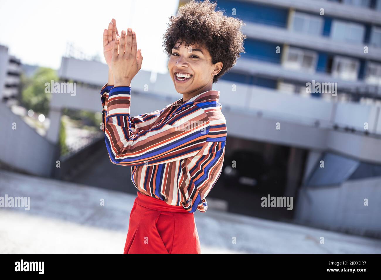 Happy woman with Afro hairstyle clapping hands at parking deck Stock ...
