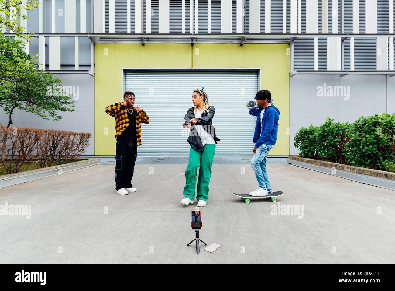 Young woman with friends filming video through smart phone in front of ...