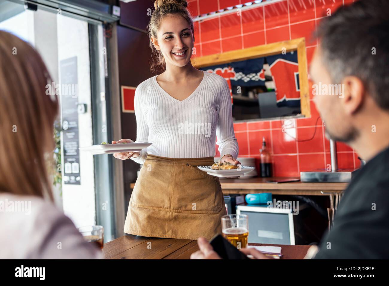 Smiling young woman in restaurant serving food to customers Stock Photo ...