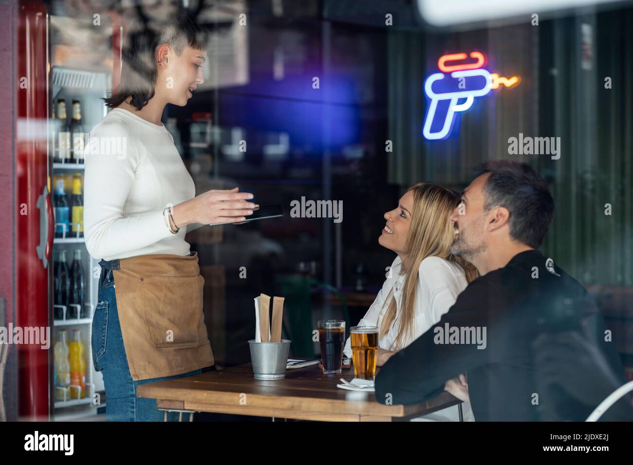 Waitress talking with customers sitting at table seen through glass ...