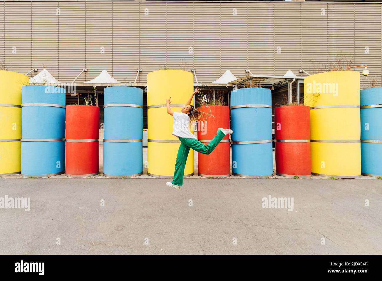 Happy young woman with arms raised jumping in front of concrete pipes ...