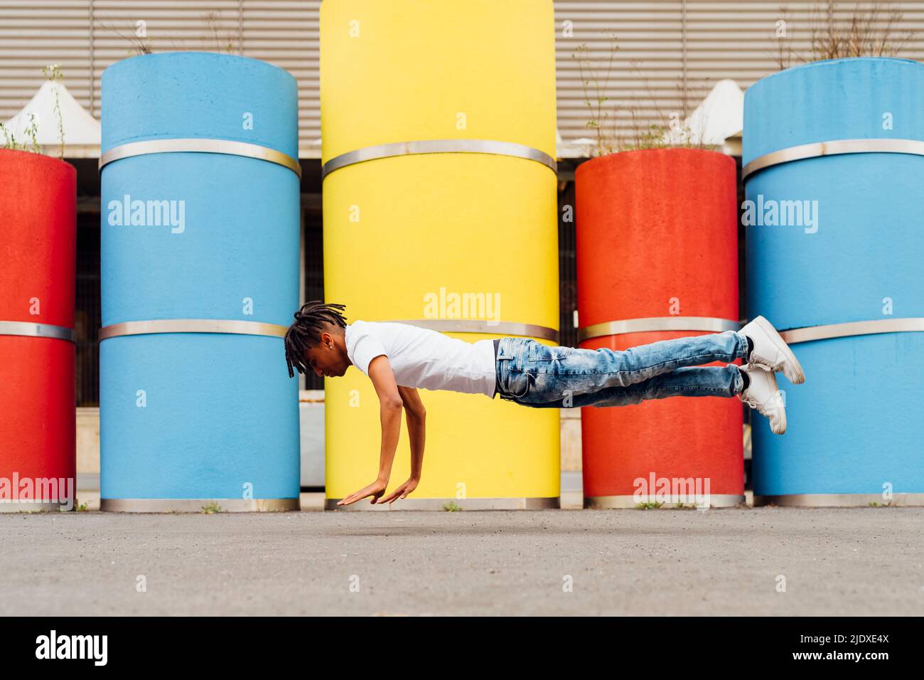 Young man in plank position jumping in front of concrete pipes Stock ...