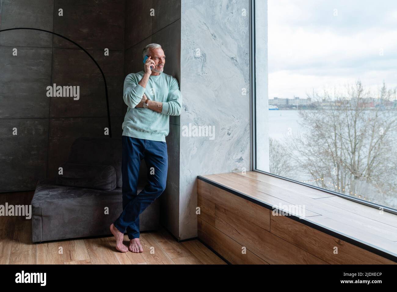Man talking on phone standing by window at home Stock Photo - Alamy