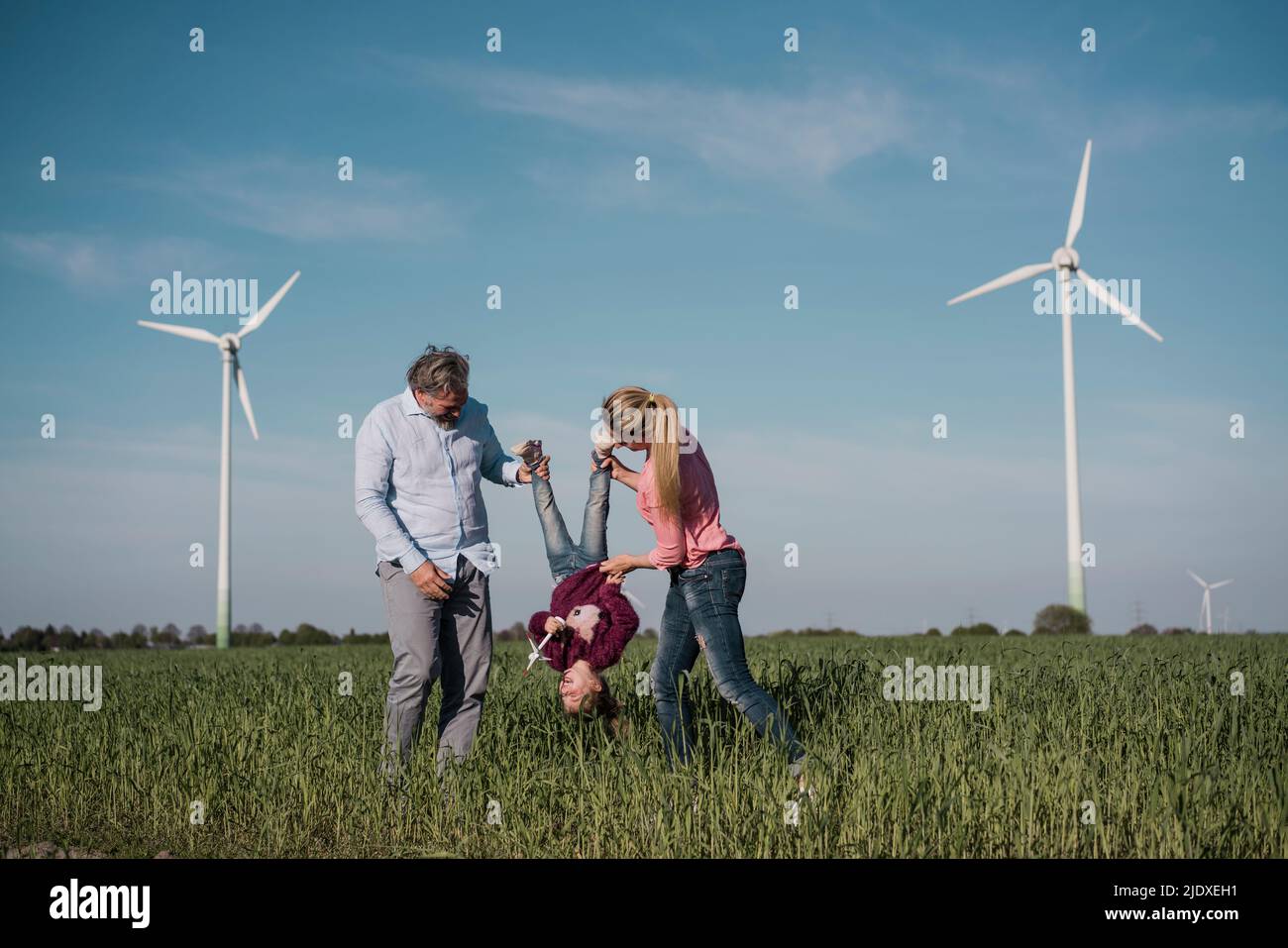 Playful parents carrying daughter upside down with wind turbines in ...