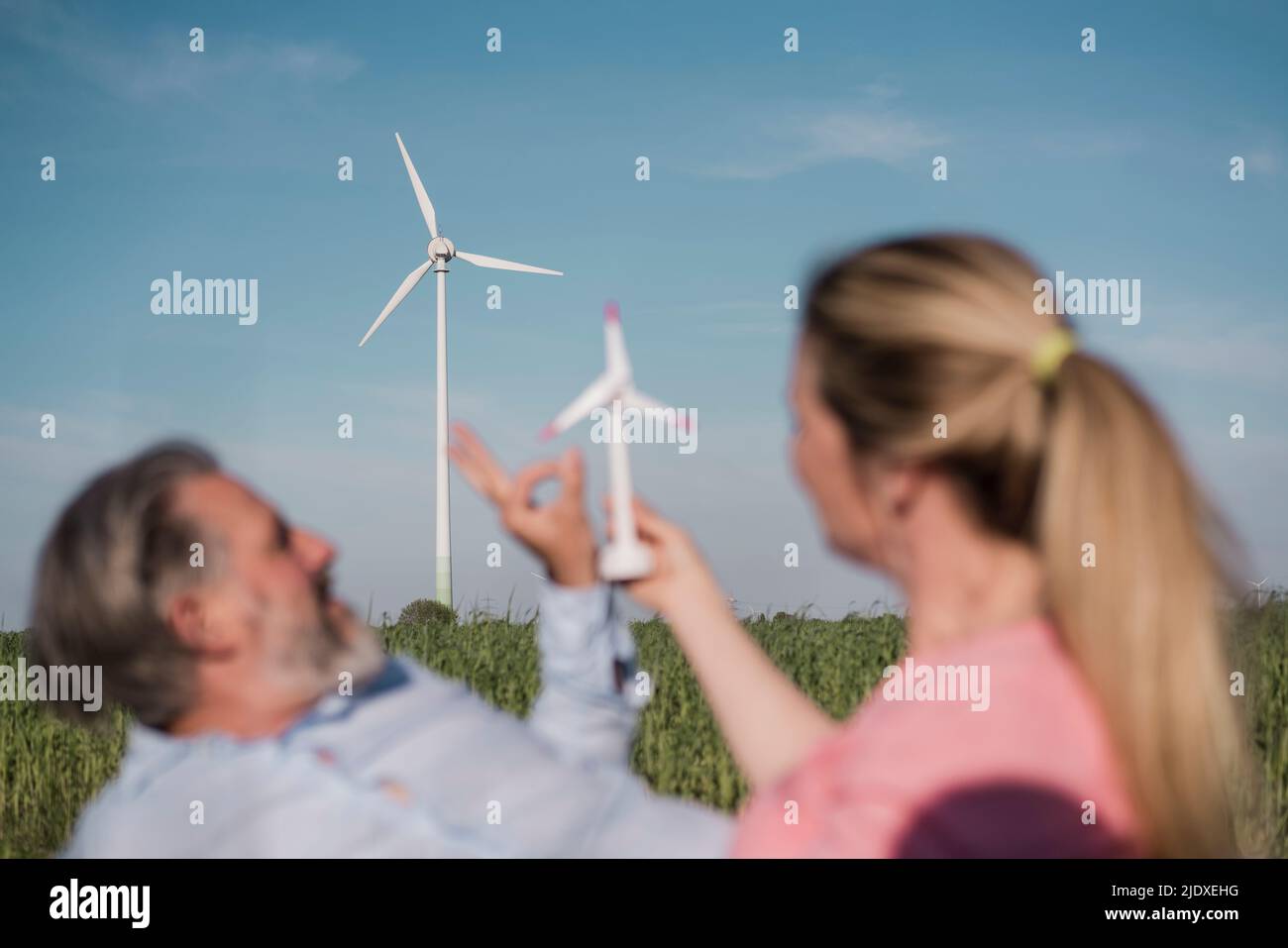 Woman holding windm turbine model sitting with man in field Stock Photo ...