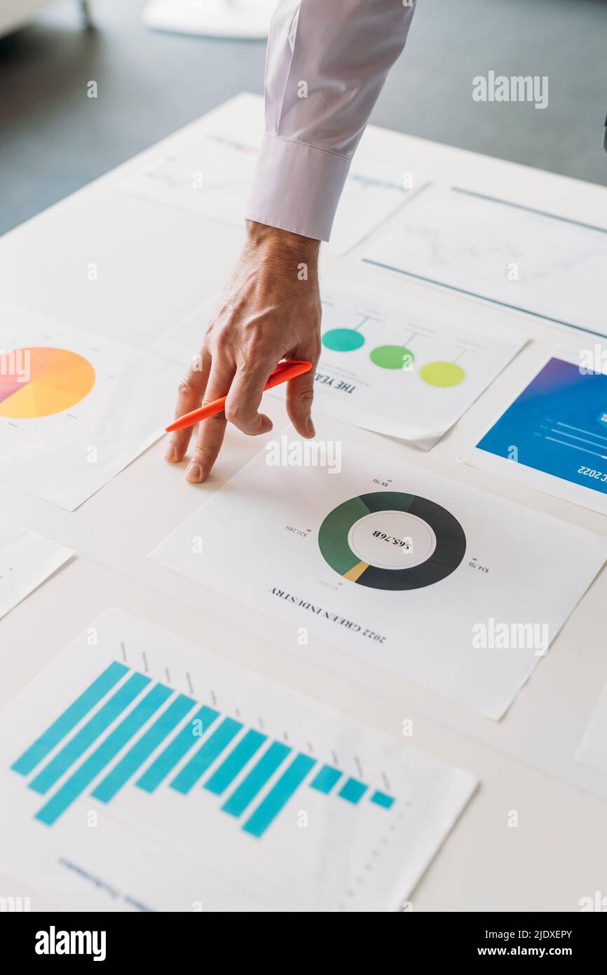 Hand of businessman with pen analyzing charts and graphs at desk in ...