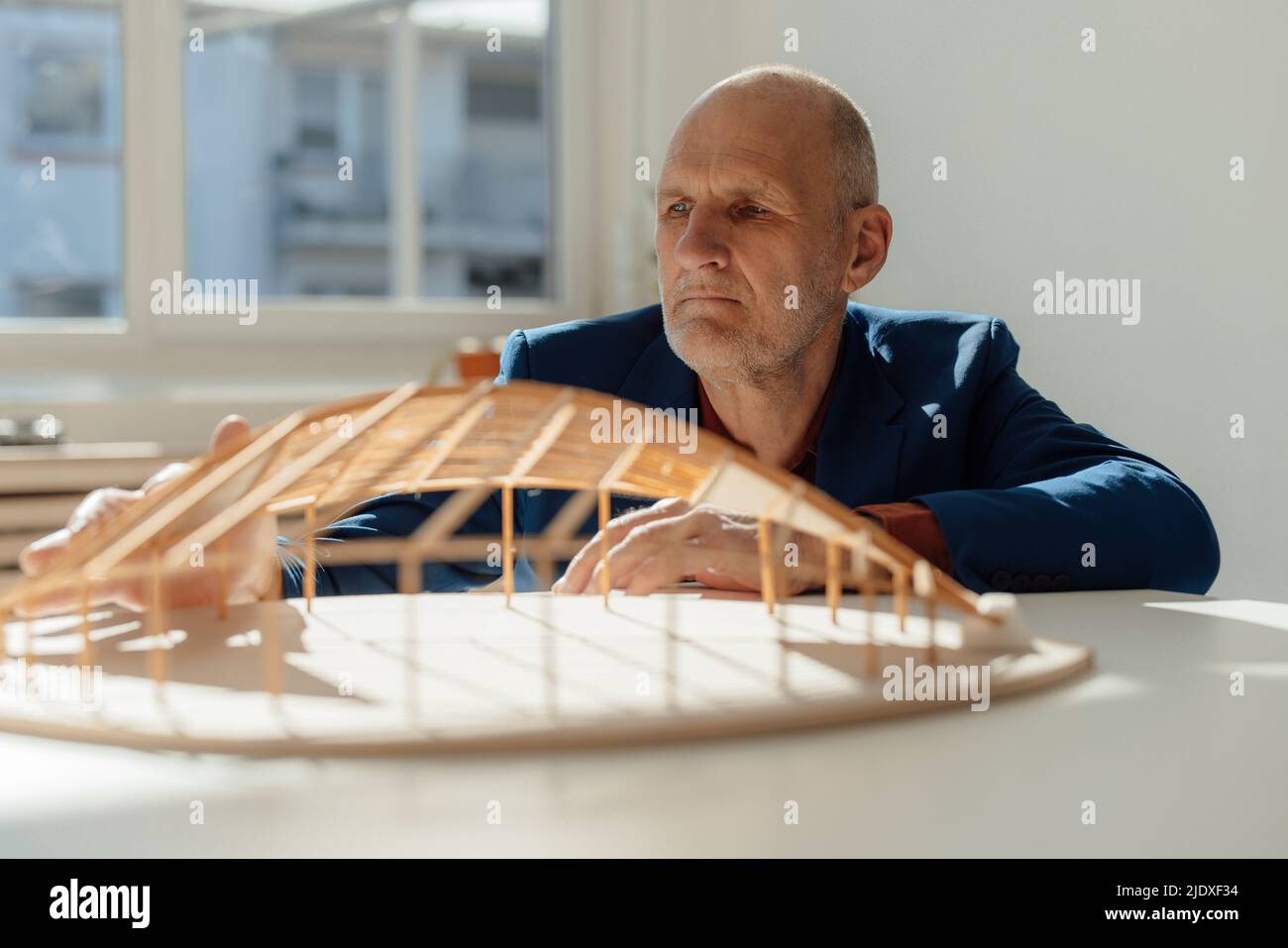 Senior architect analyzing leaf shape wooden model at desk in office ...