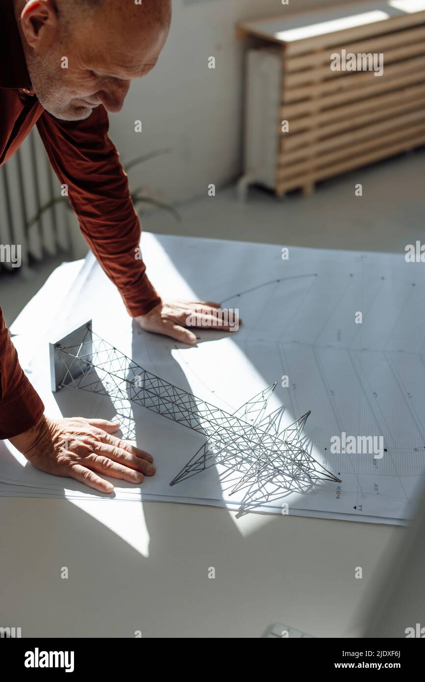 Senior engineer looking at electricity pylon model on blueprint at desk ...