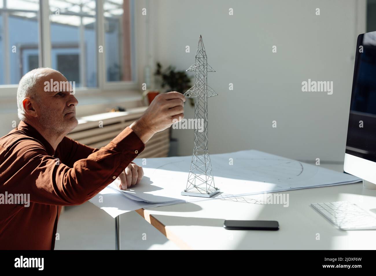 Businessman analyzing electricity pylon model on blueprint at desk ...
