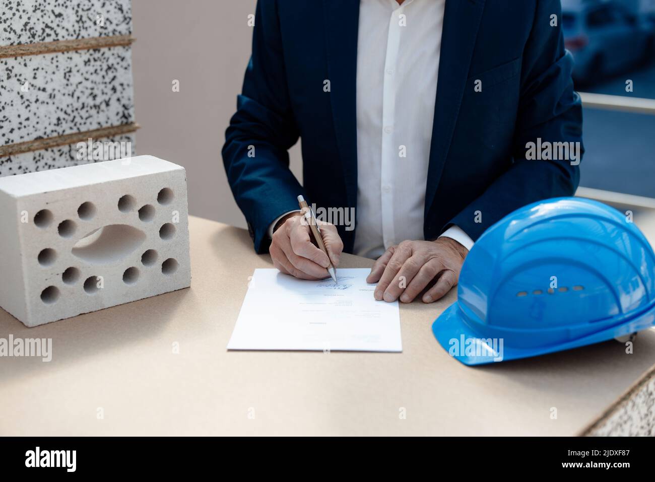 Senior businessman signing document amidst concrete brick and hardhat ...