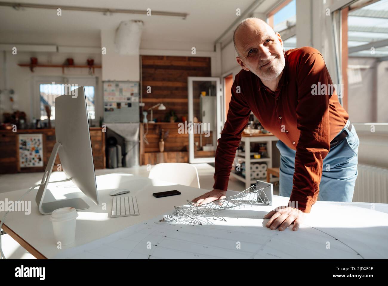 Smiling engineer with electricity pylon model and blueprint at desk in ...