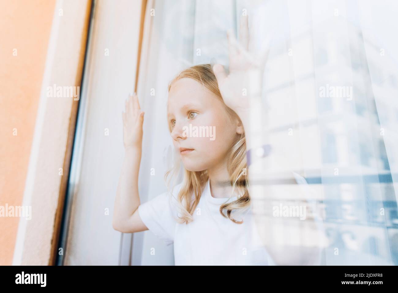Contemplative girl looking through glass window at home Stock Photo - Alamy