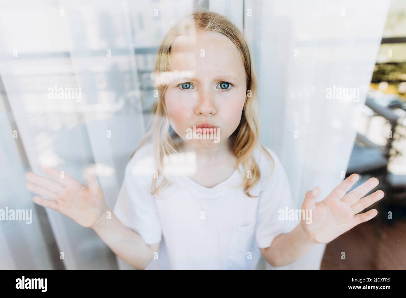 Worried girl standing by glass window at home Stock Photo - Alamy