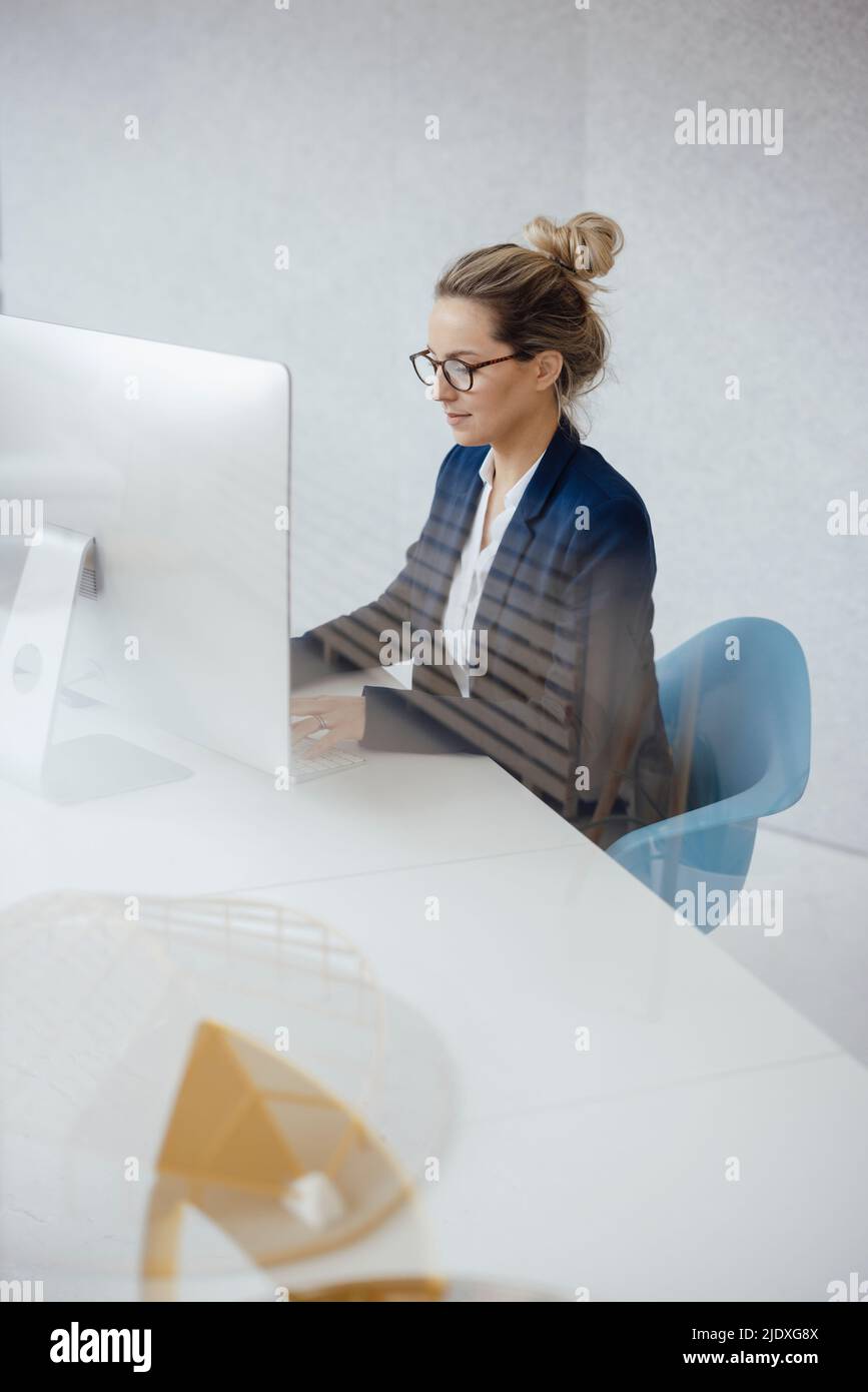 Businesswoman using desktop PC at desk seen through glass Stock Photo ...
