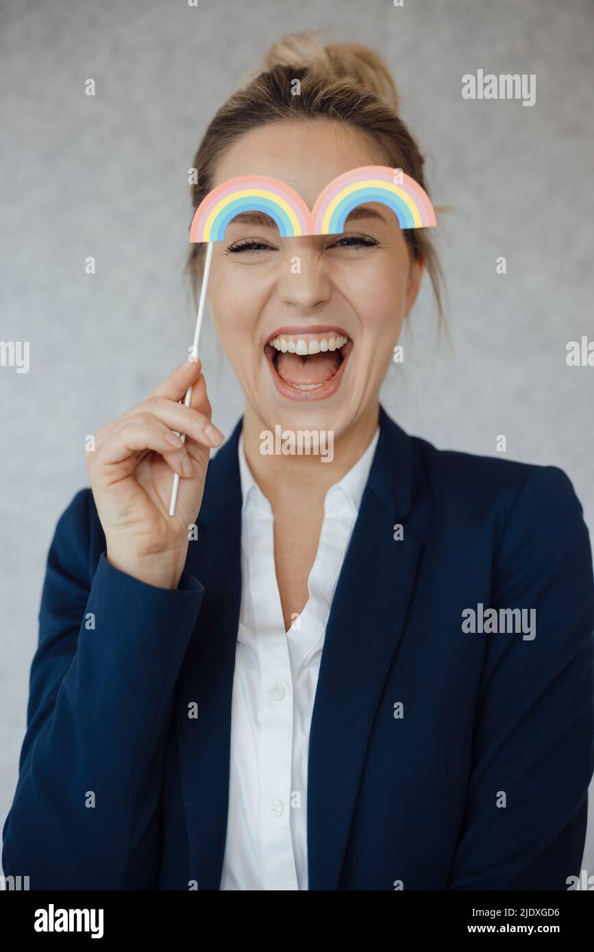 Happy businesswoman holding rainbow prop in office Stock Photo - Alamy