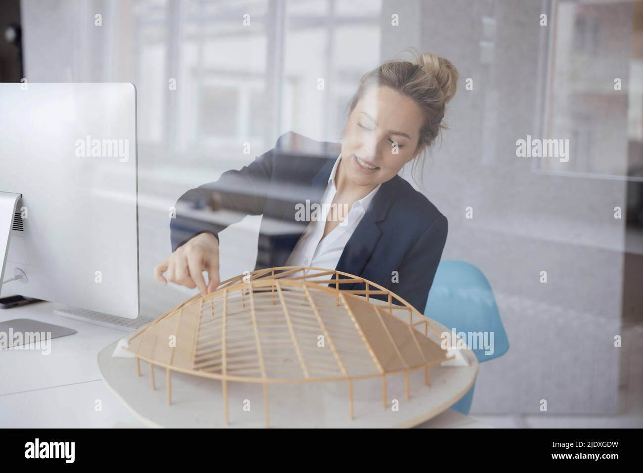 Businesswoman examining leaf shape model at desk seen through glass ...