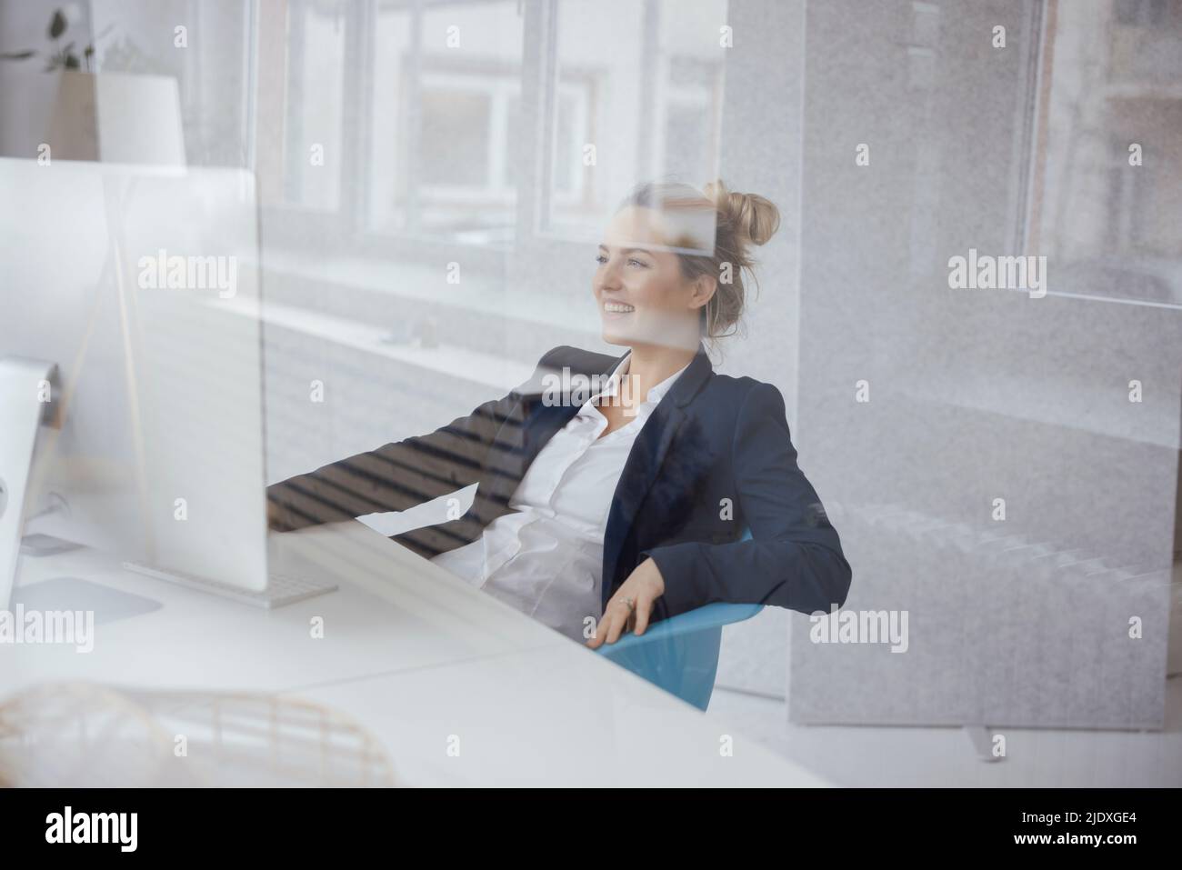 Happy businesswoman using desktop PC at desk seen through glass Stock ...