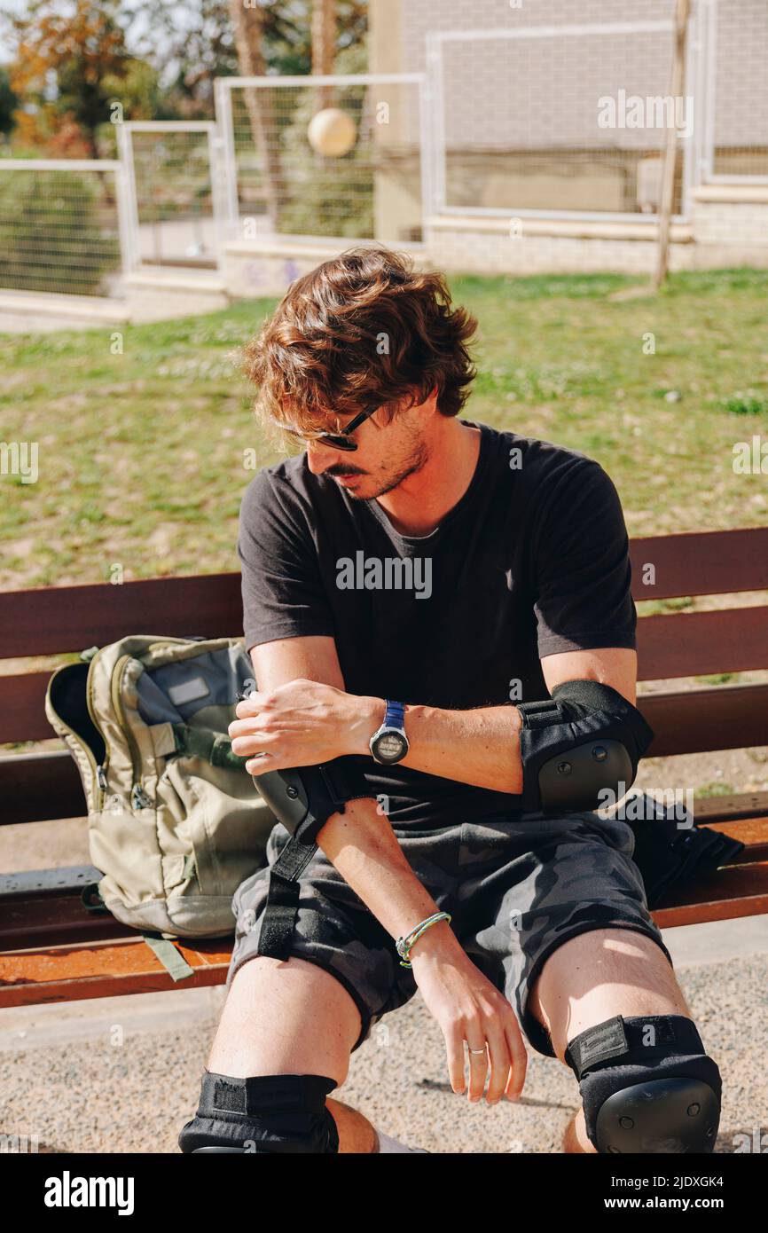 Man sitting on bench adjusting elbow pad at park Stock Photo - Alamy