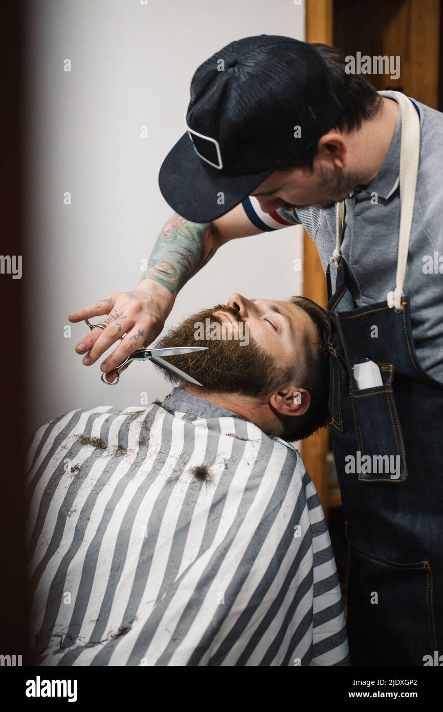 Barber trimming up clients beard in salon Stock Photo - Alamy