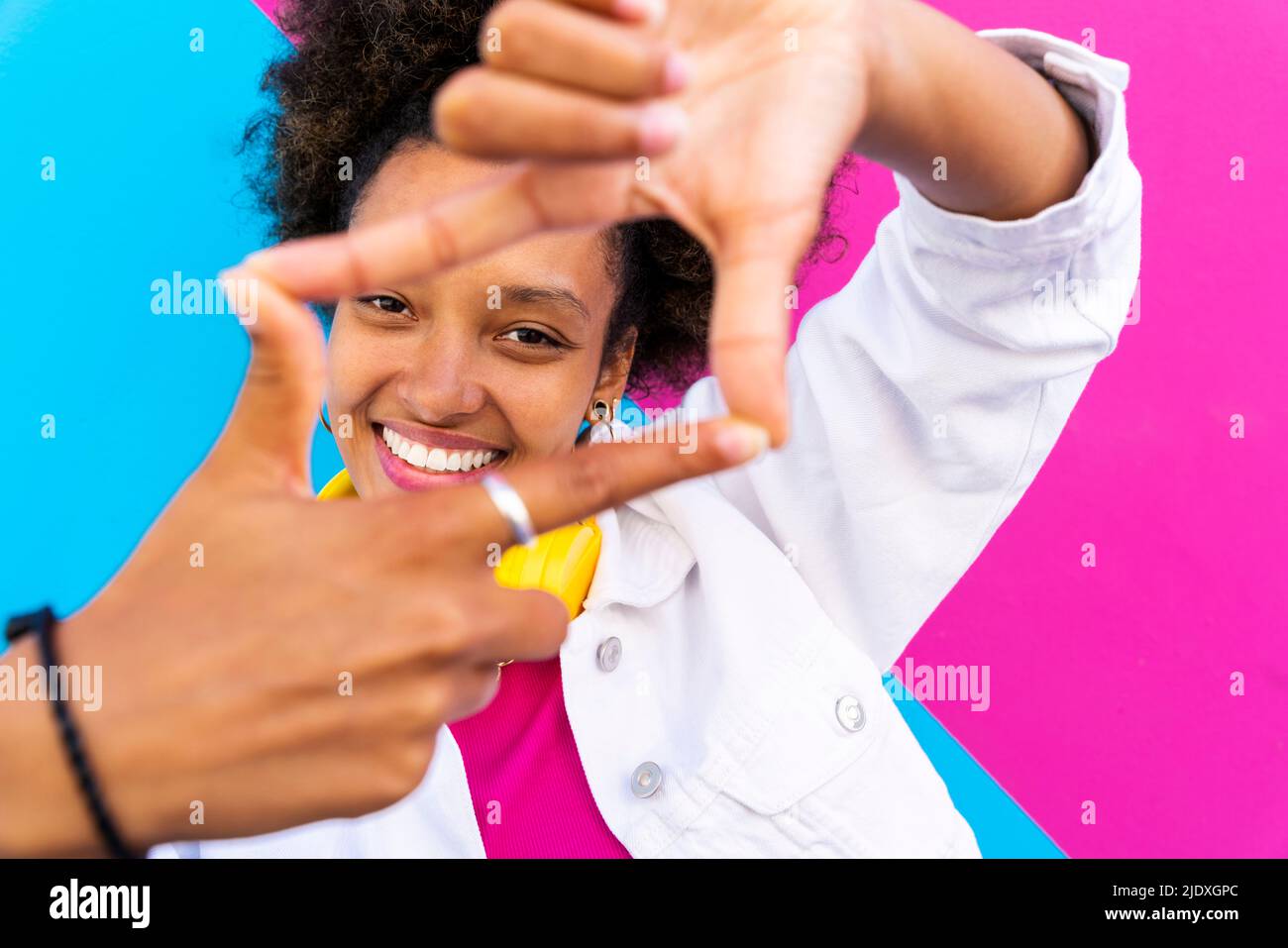 Happy young woman gesturing finger frame in front of pink and blue wall ...
