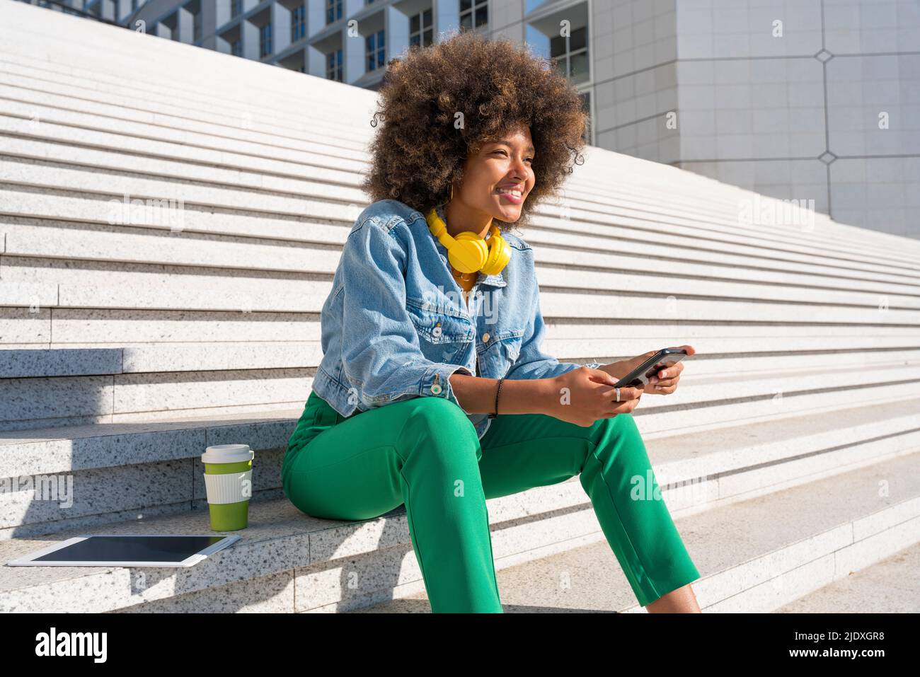 Smiling Afro Woman Wearing Wireless Headphones Sitting With Mobile