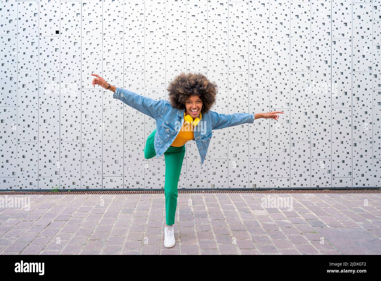 Happy Afro woman with arms outstretched standing on one leg in front of ...