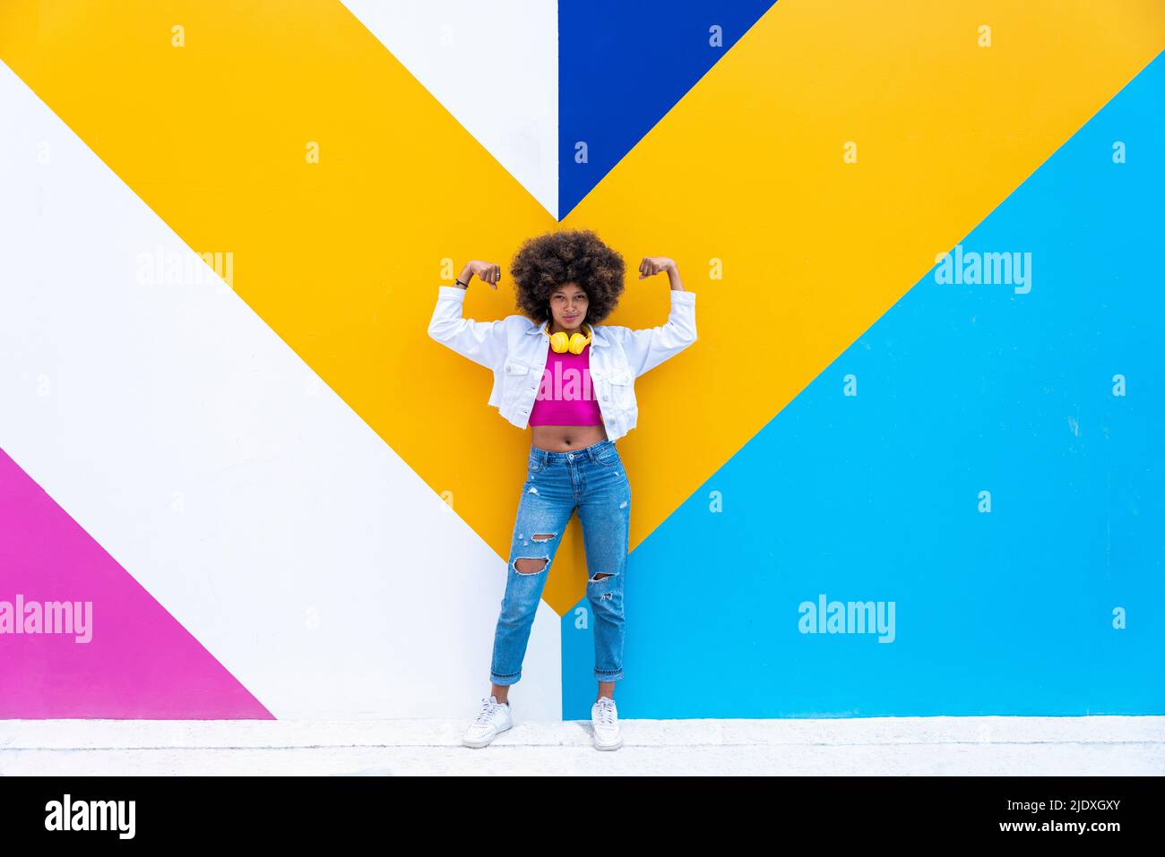 Afro woman flexing muscles in front of colorful wall Stock Photo - Alamy