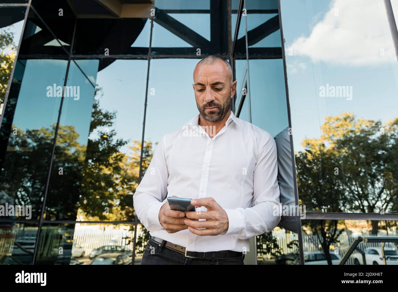 Man using smart phone leaning against glass wall Stock Photo - Alamy