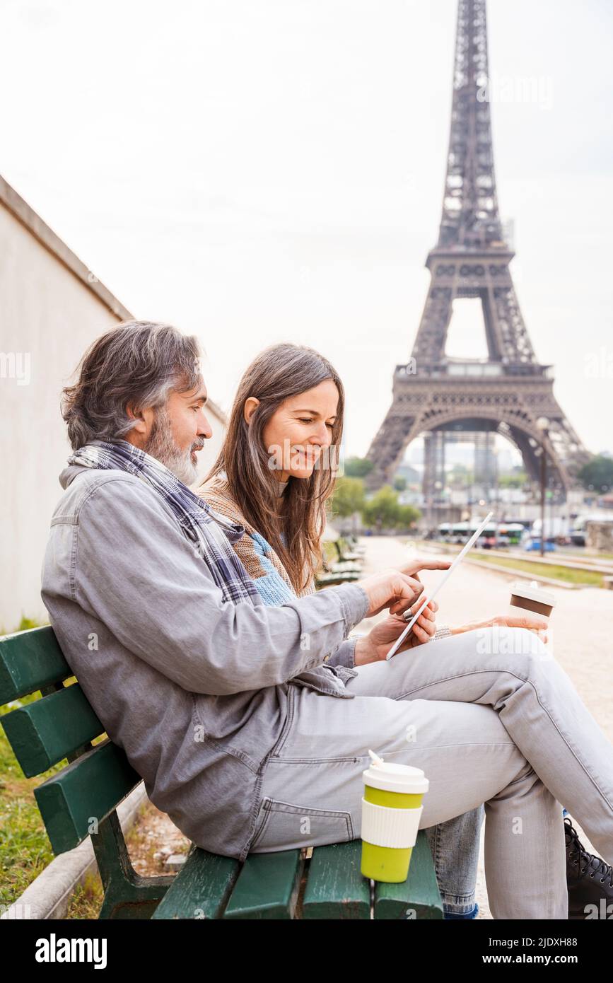 Smiling woman with man using tablet PC sitting on bench near Eiffel ...