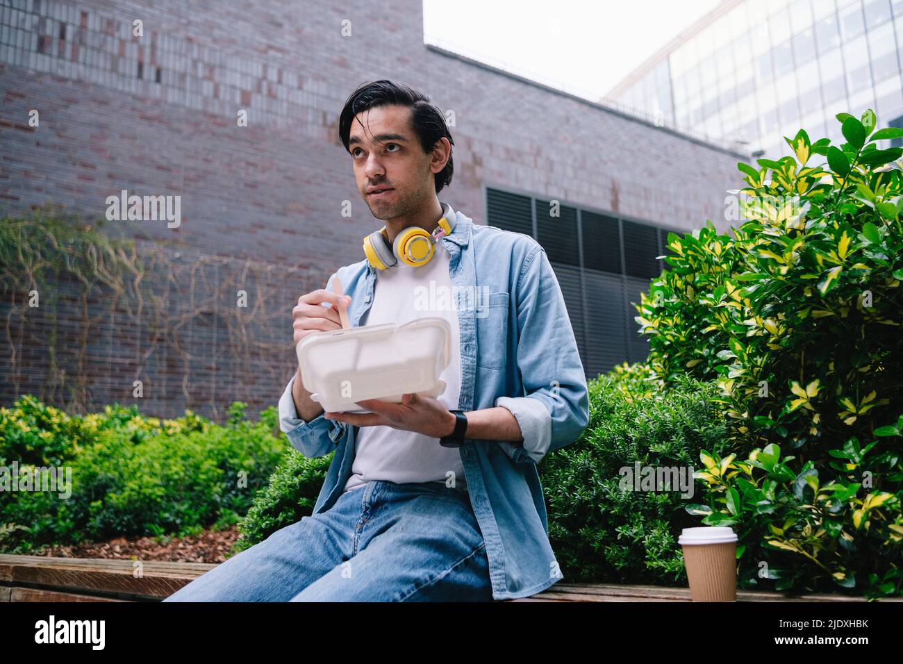 Man eating takeaway food sitting near plants Stock Photo - Alamy