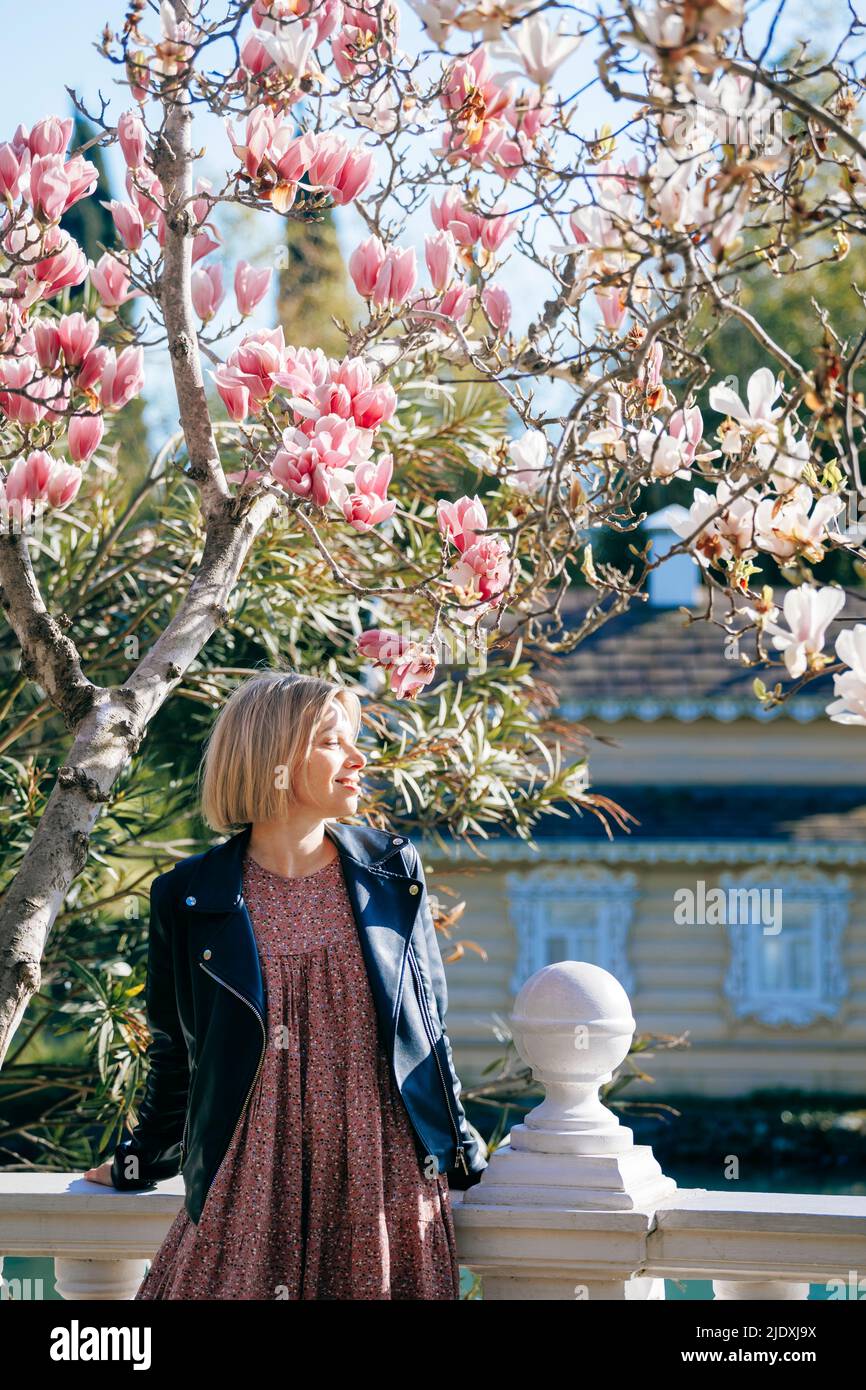 Woman standing under tree with pink flowers by railing Stock Photo - Alamy
