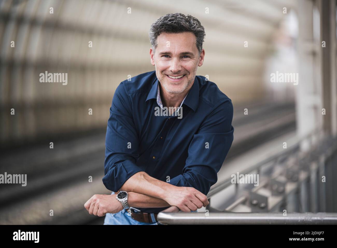 Smiling mature man leaning on railing at railroad station Stock Photo ...