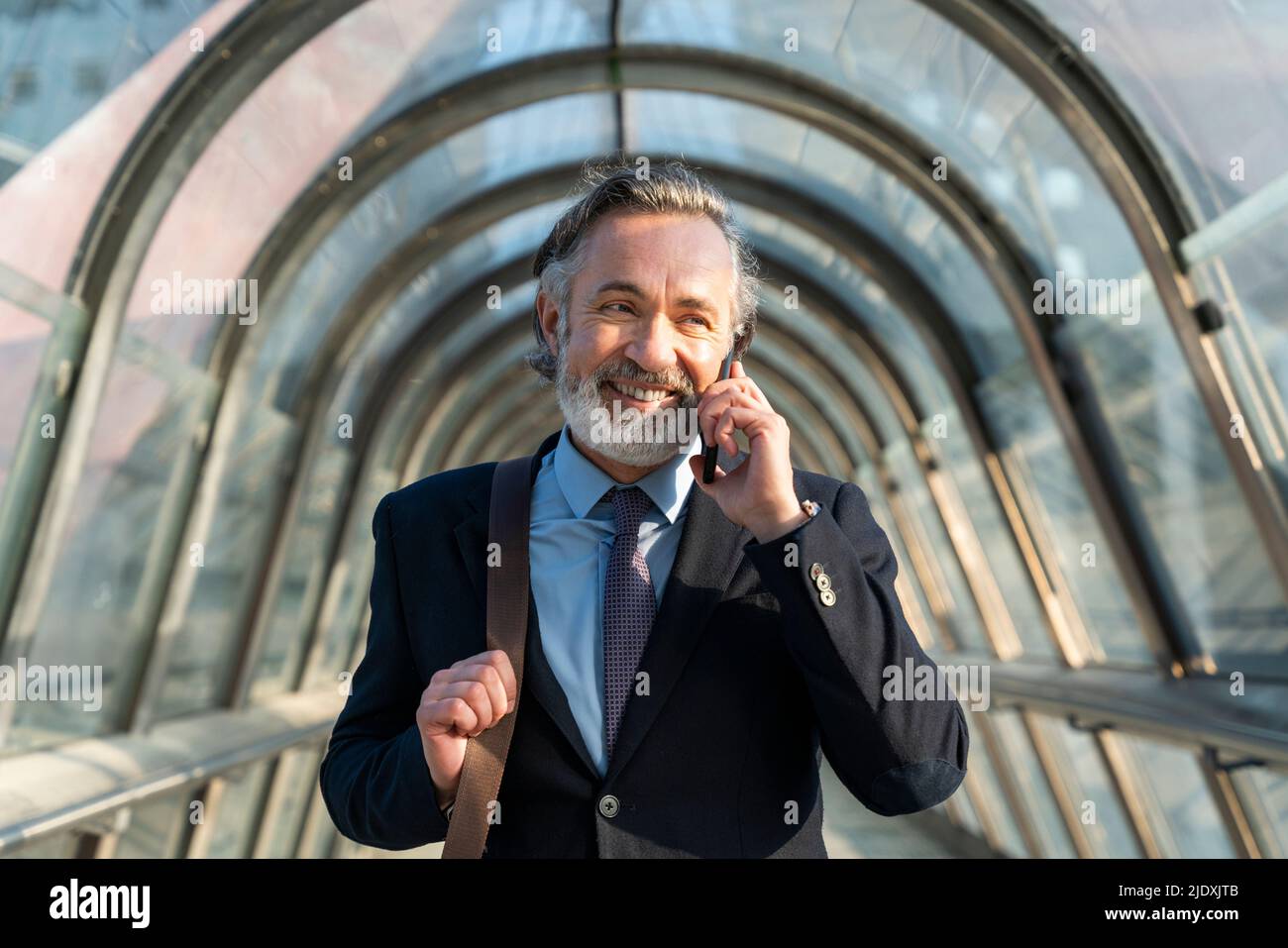 Happy mature businessman talking through smart phone on footbridge ...