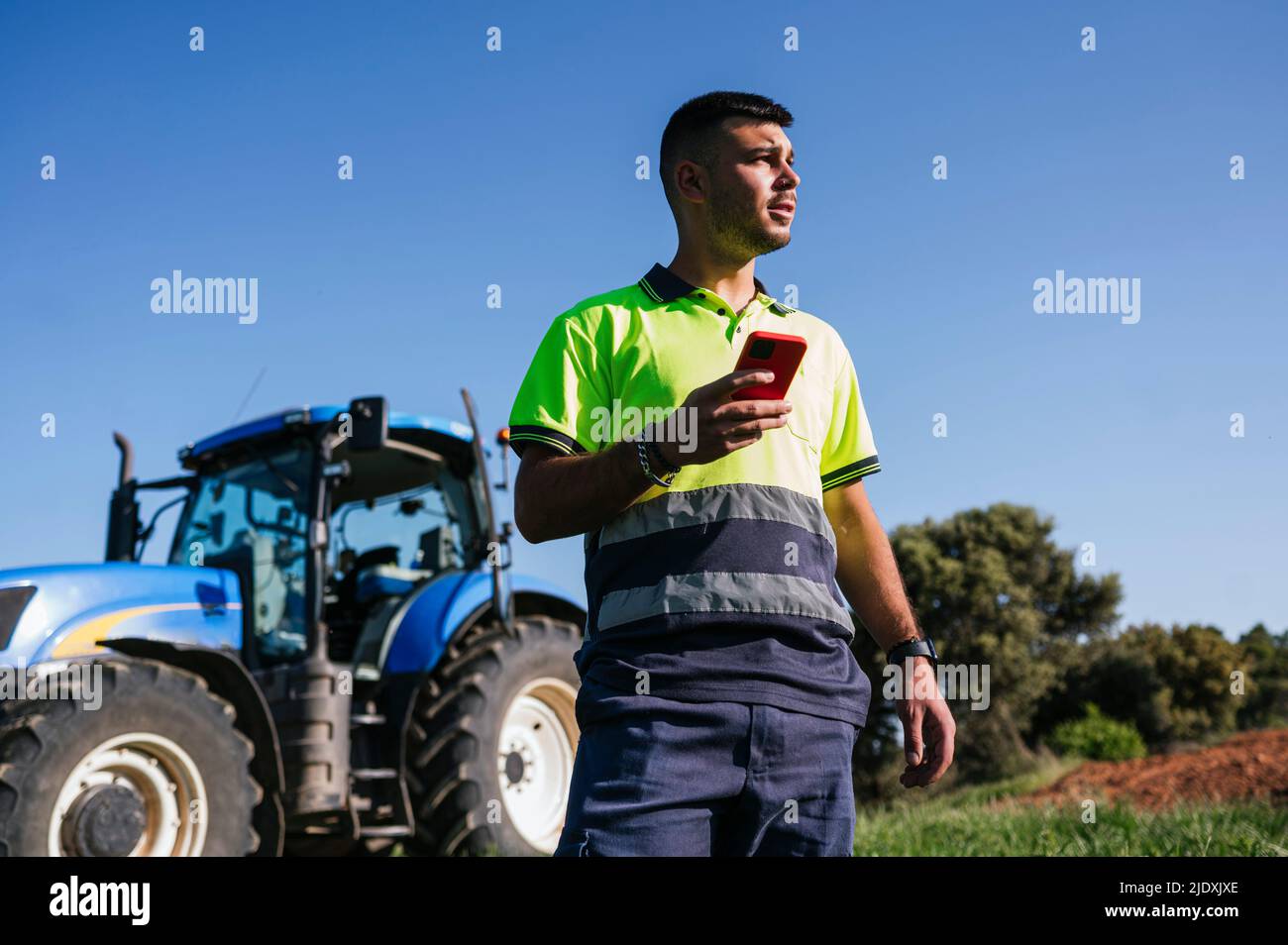 Farmer holding mobile phone in front of tractor Stock Photo - Alamy