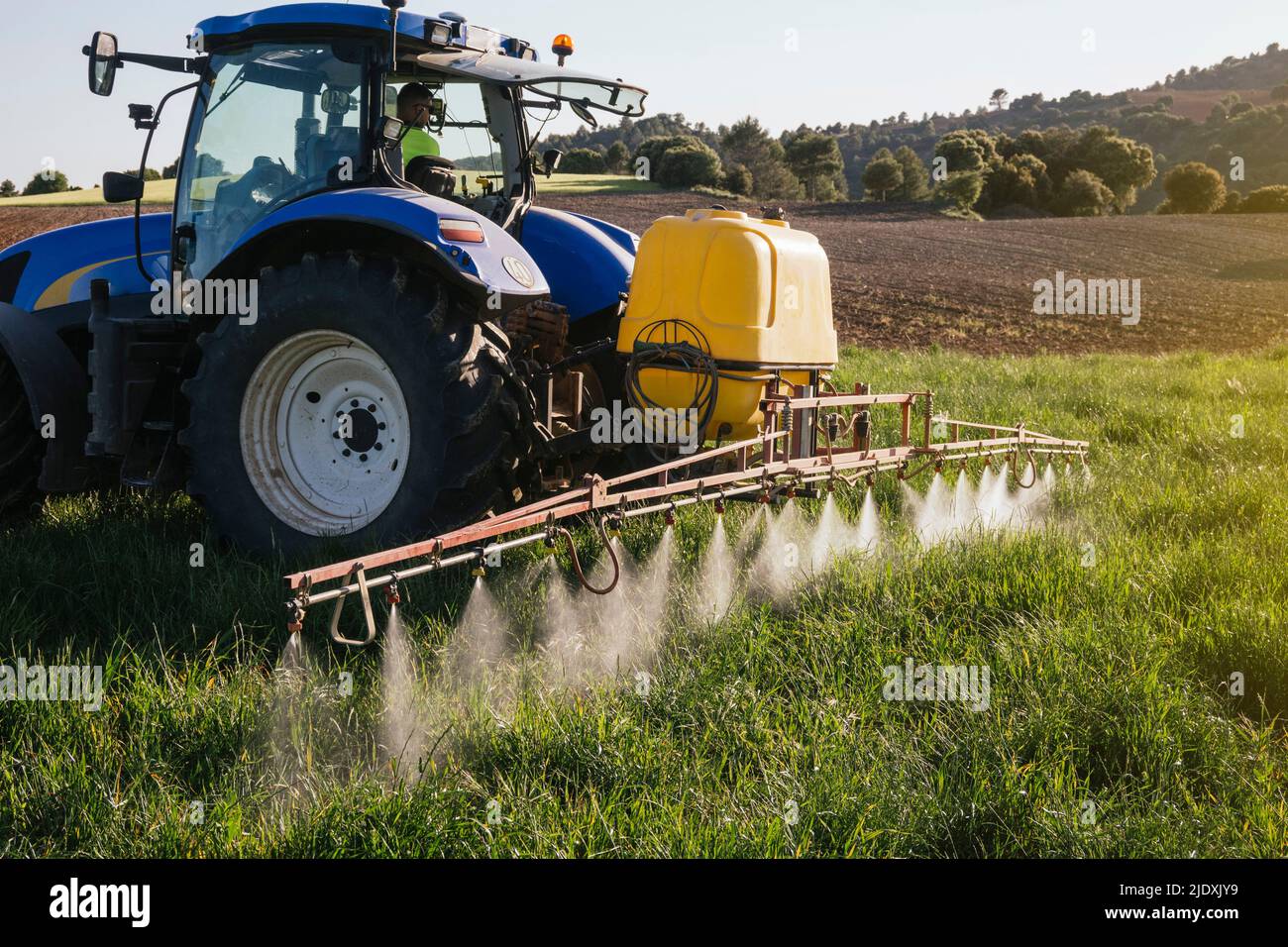 Farmer spraying fertilizer through sprayer sitting in tractor on field ...