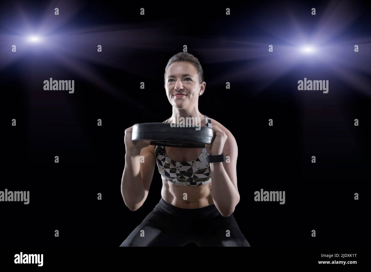 Smiling young woman lifting weight plate in fitness room Stock Photo ...