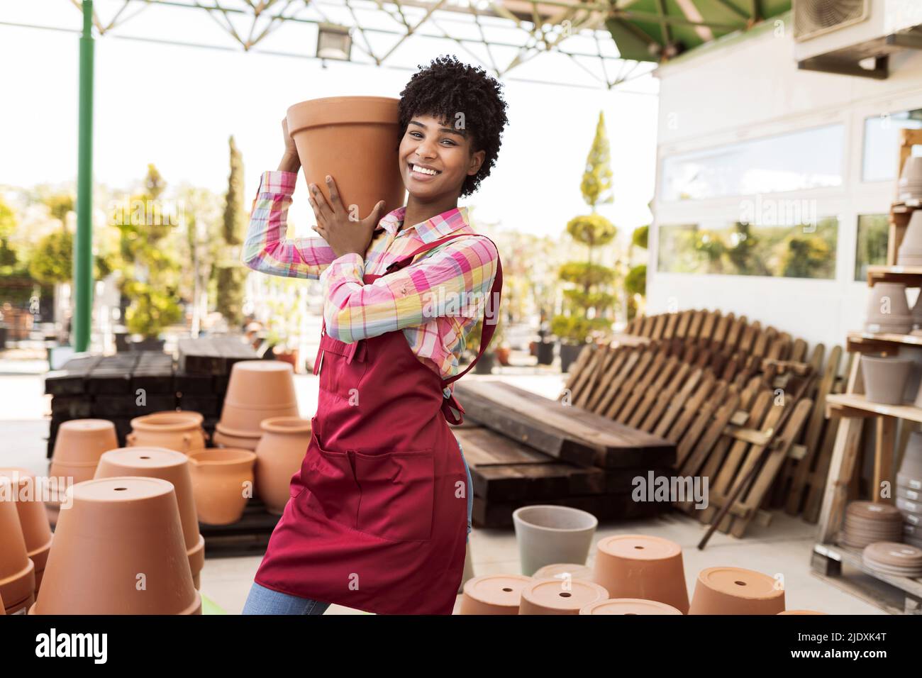 Smiling gardener carrying pot standing in warehouse Stock Photo - Alamy