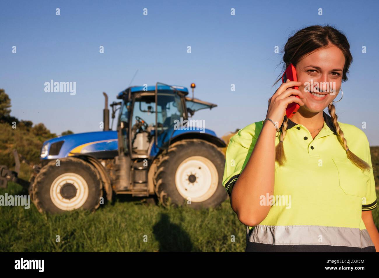 Smiling female farmer talking on mobile phone standing in front of ...